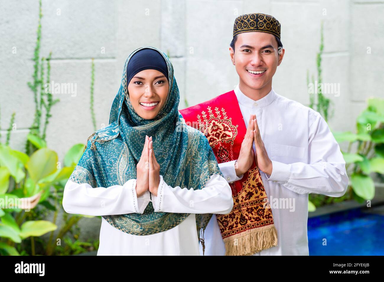 Asian Muslim man and woman welcoming guests wearing traditional dress ...