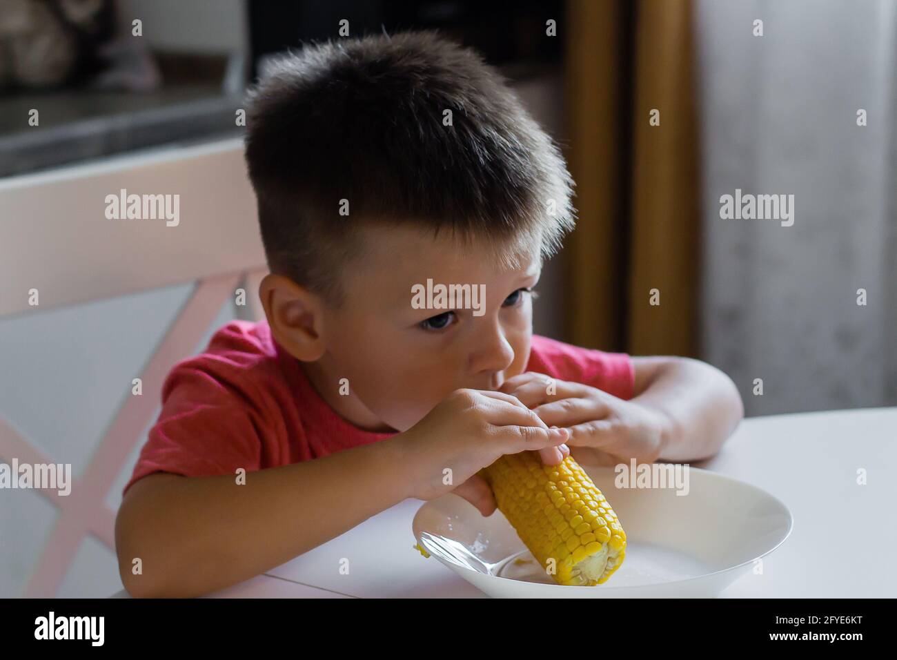 Little boy eats corn at the kitchen Stock Photo - Alamy