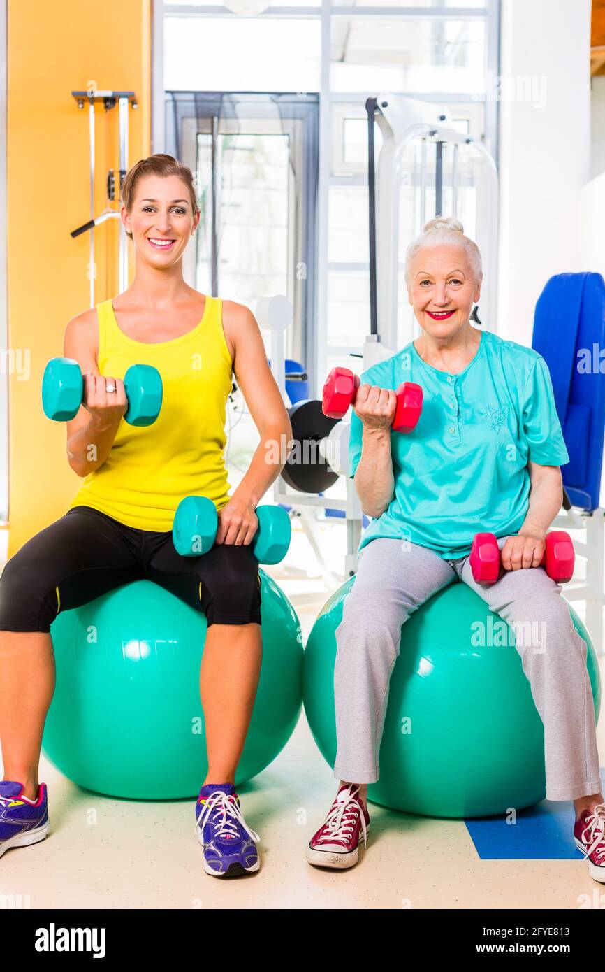 Senior and young woman on fitness ball doing sport having dumbbell ...