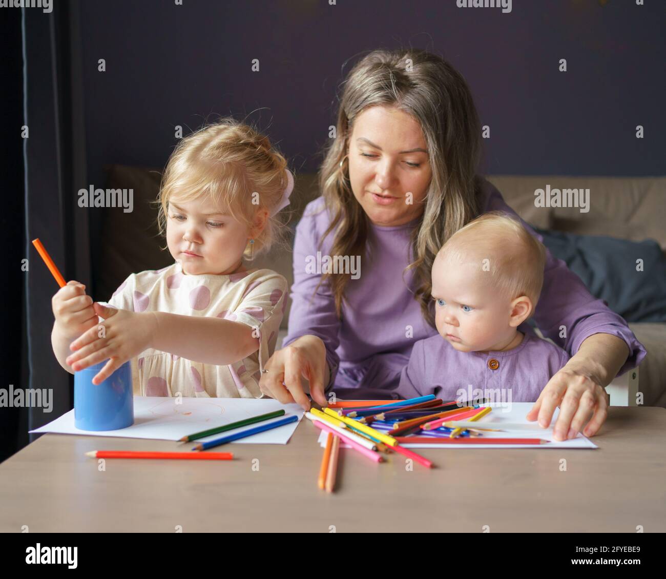 Young loving mother drawing with colored pencils with two adorable ...