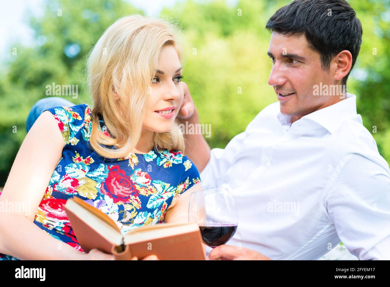 Couple drinking wine reading book on meadow Stock Photo - Alamy