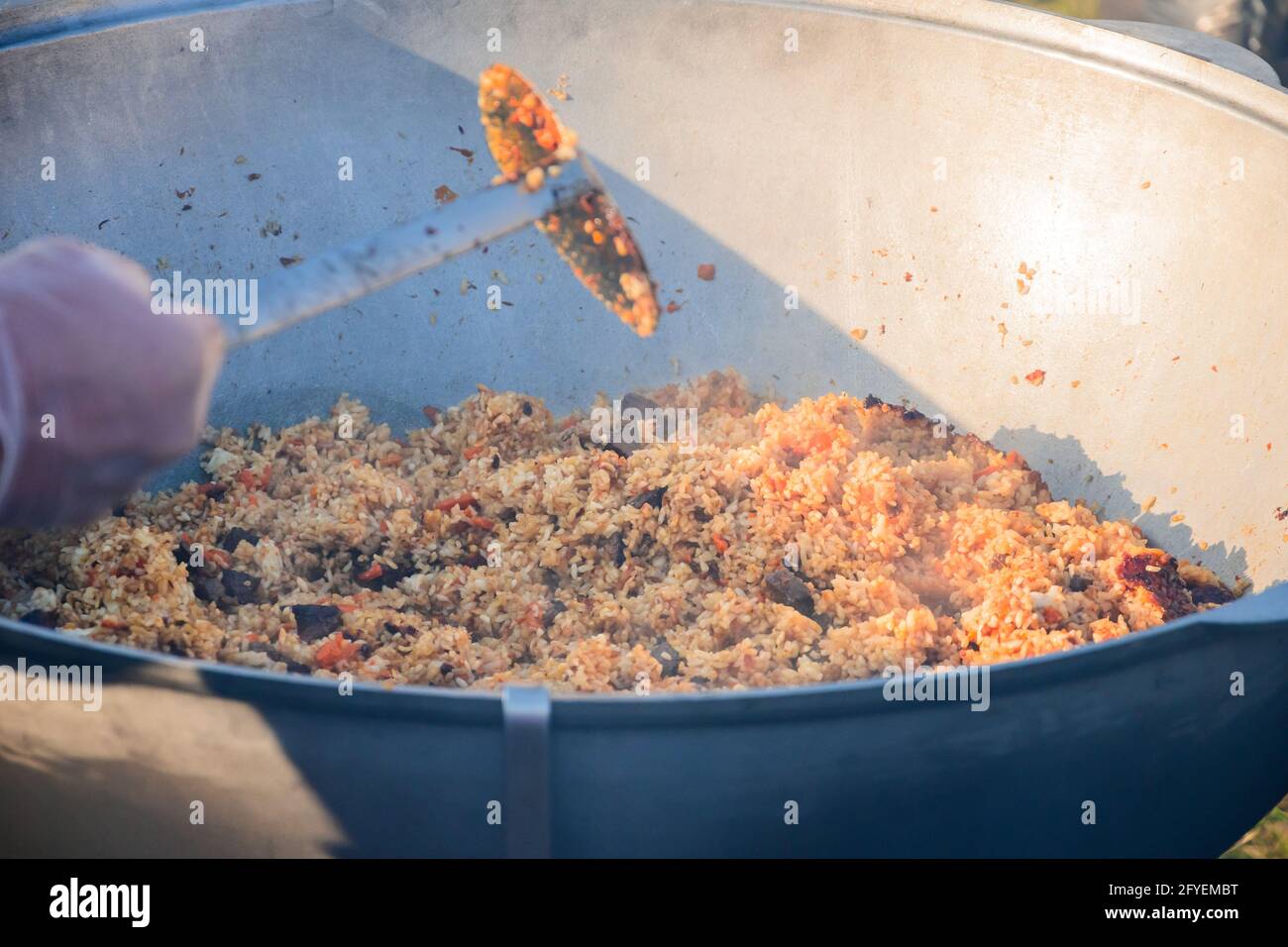 Hot pilaf in a large cauldron on the stove in the park. Traditional ...