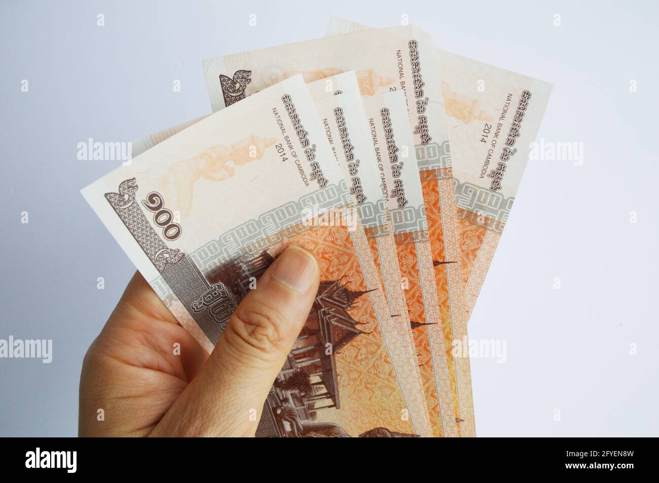 Cropped hand holding multiple 100 riel, Cambodia currency in white ...