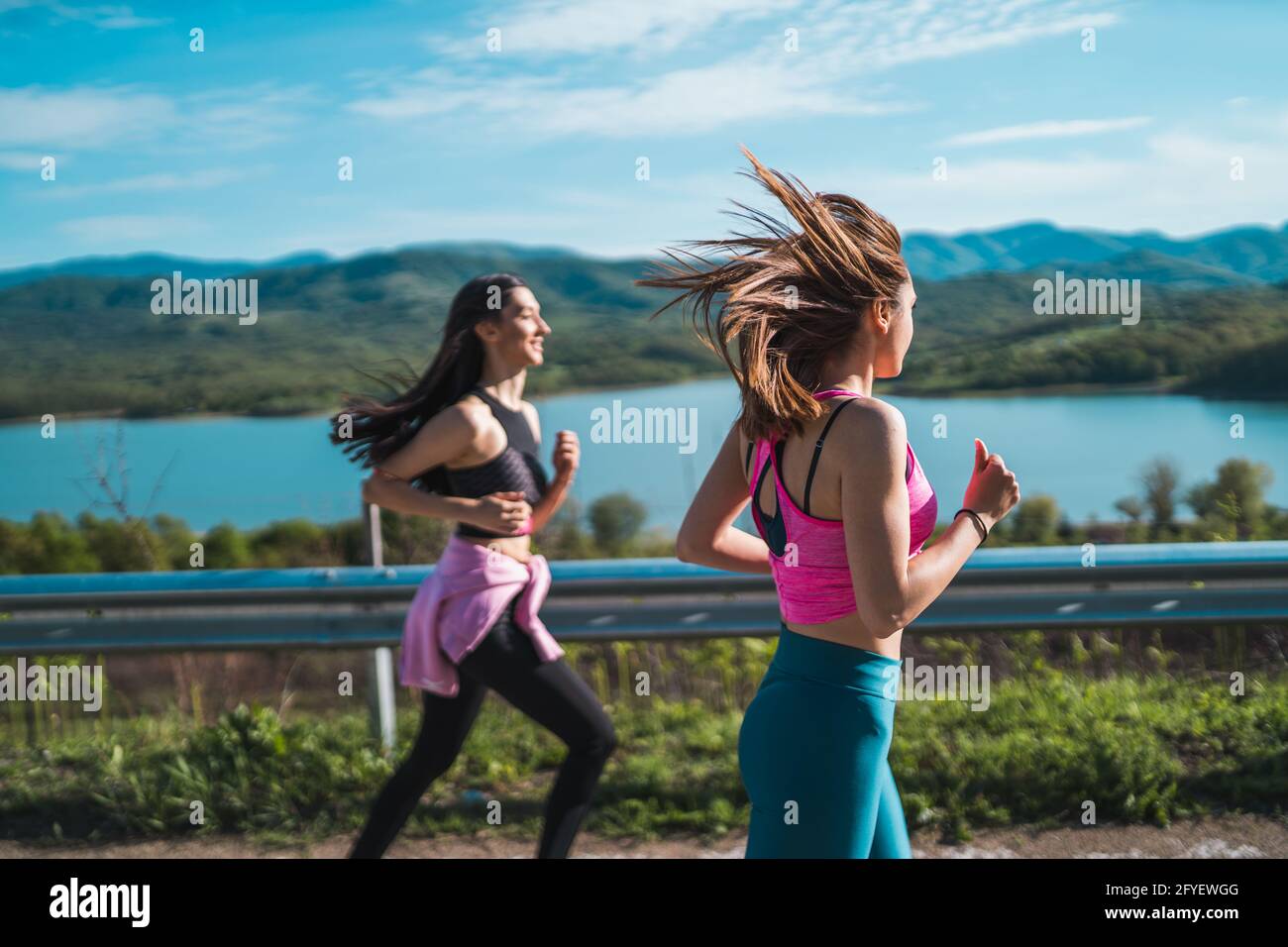 Two beautiful happy fit girls running outdoors in sunny day, keeping ...