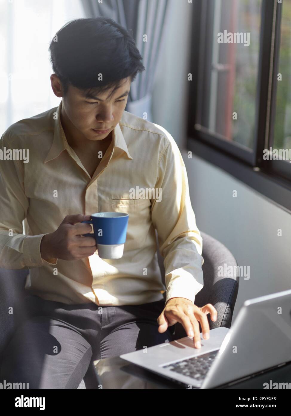 Young businessman working with laptop computer while holding a cup of ...