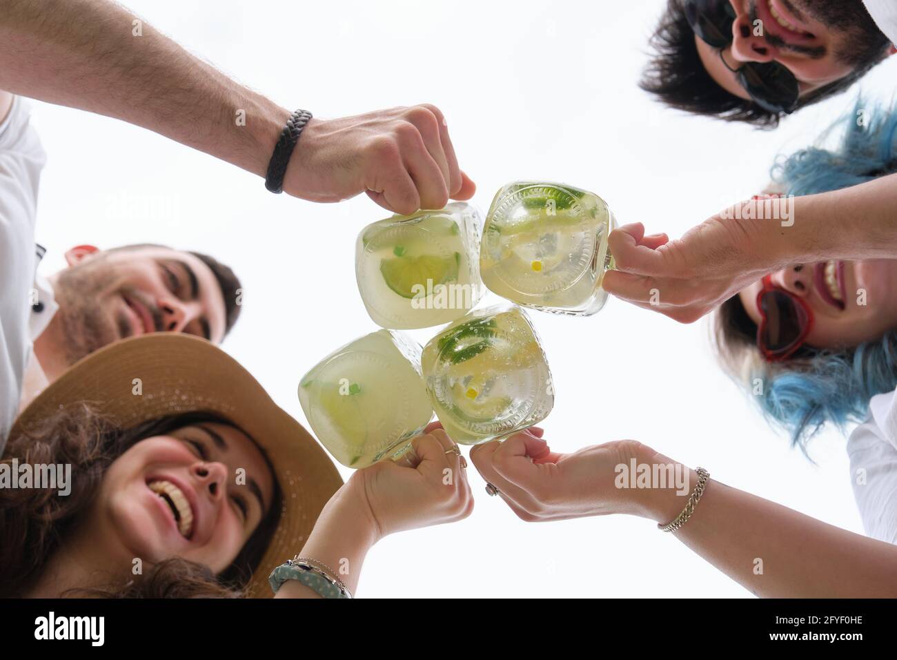 Group of four friends smiling and toasting with refreshing drinks over ...