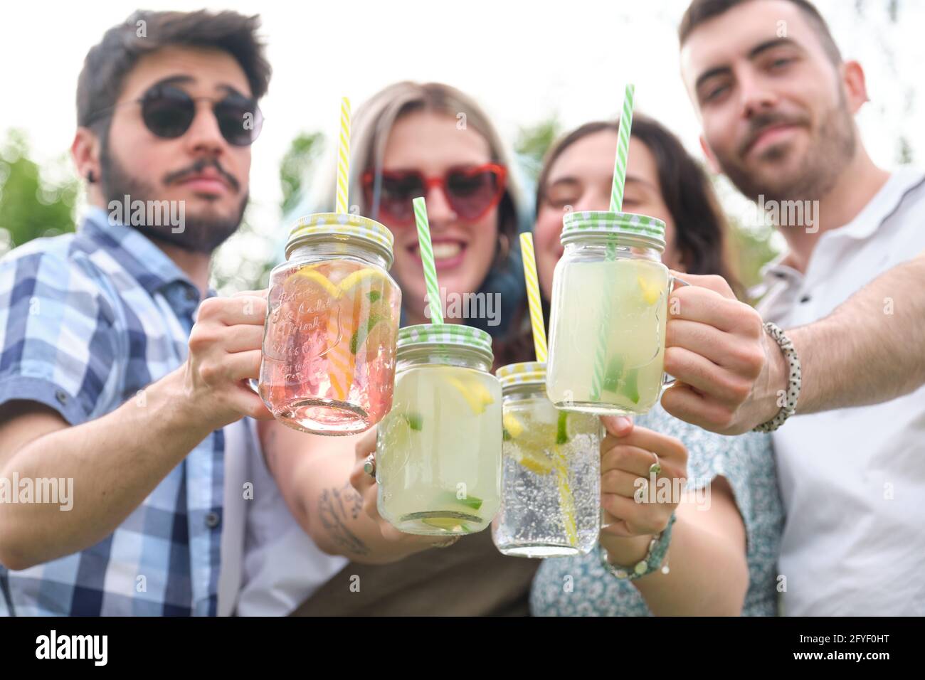 Group of four friends smiling and toasting with refreshing drinks ...