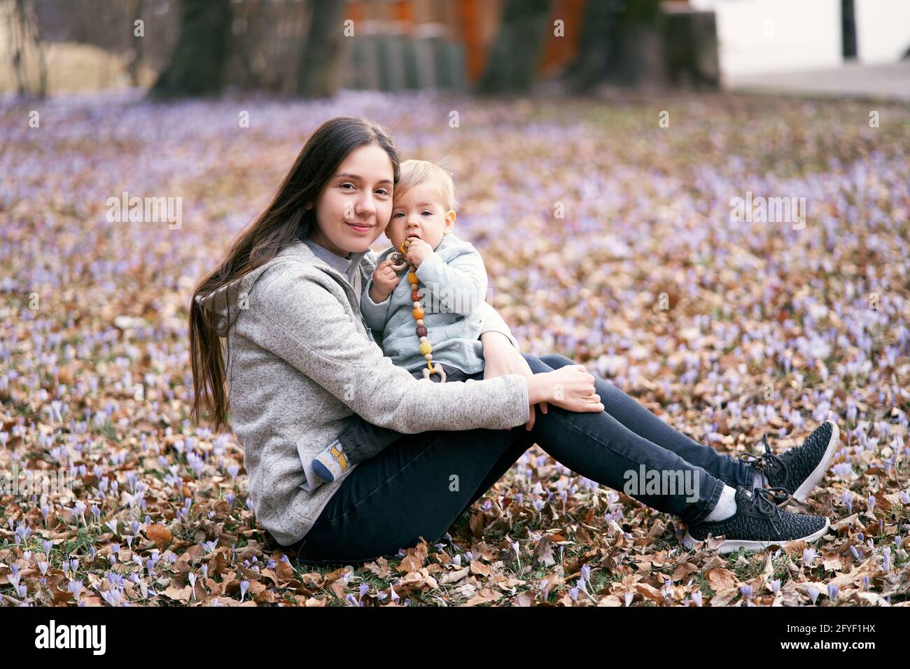 Smiling mom sitting on leaves in the park hugging cute baby she is ...