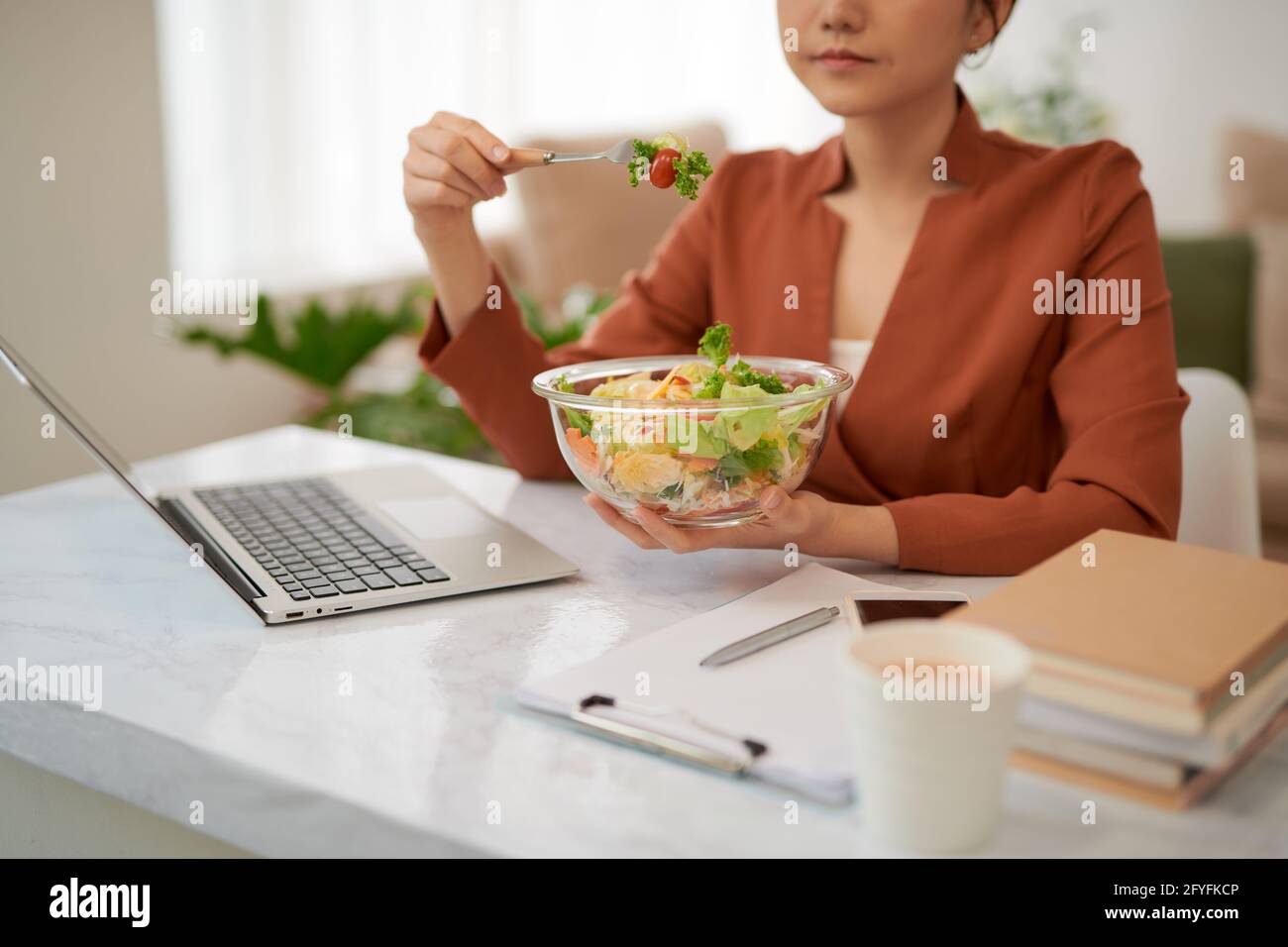 woman with laptop in modern office interior, eating lunch Stock Photo ...