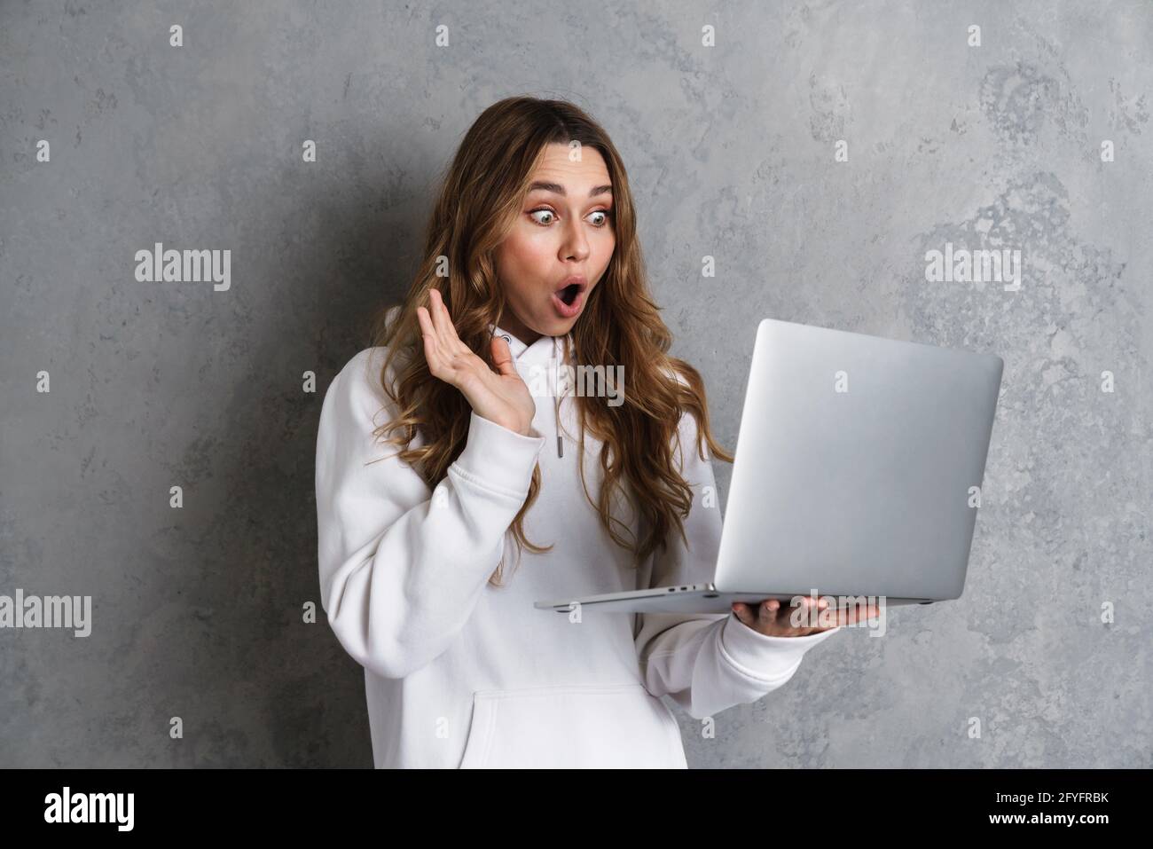 Portrait of a shocked woman holding laptop computer while standing ...