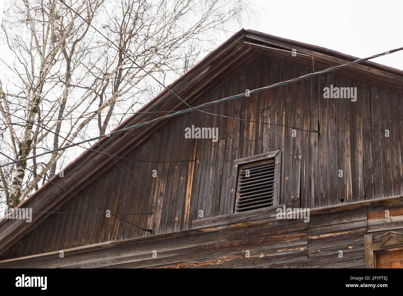 Wooden technical window under the roof of an old planked building. An ...