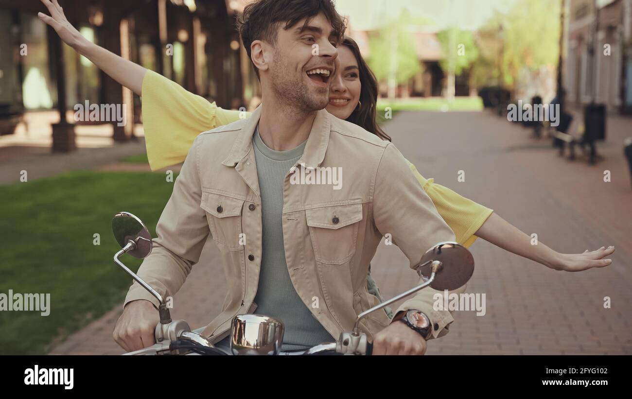 excited man and happy woman with outstretched hands riding motorcycle ...