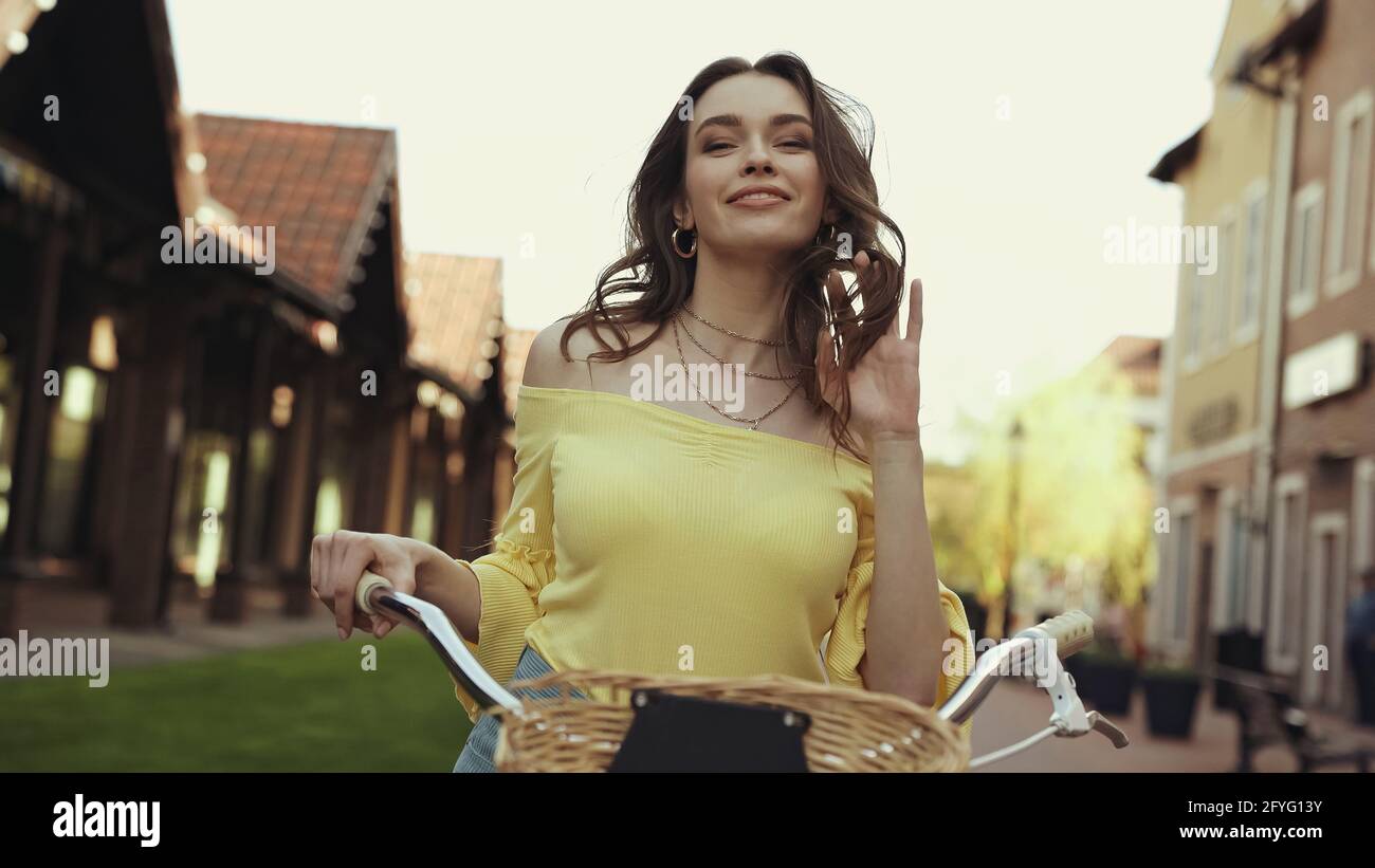 happy young woman with wavy hair smiling while riding bike outside ...
