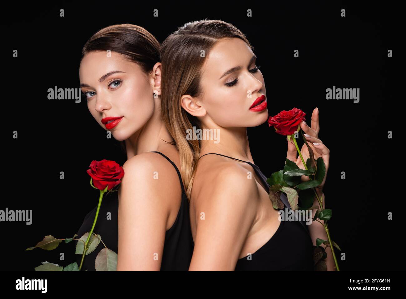 seductive women holding red roses while standing back to back isolated ...