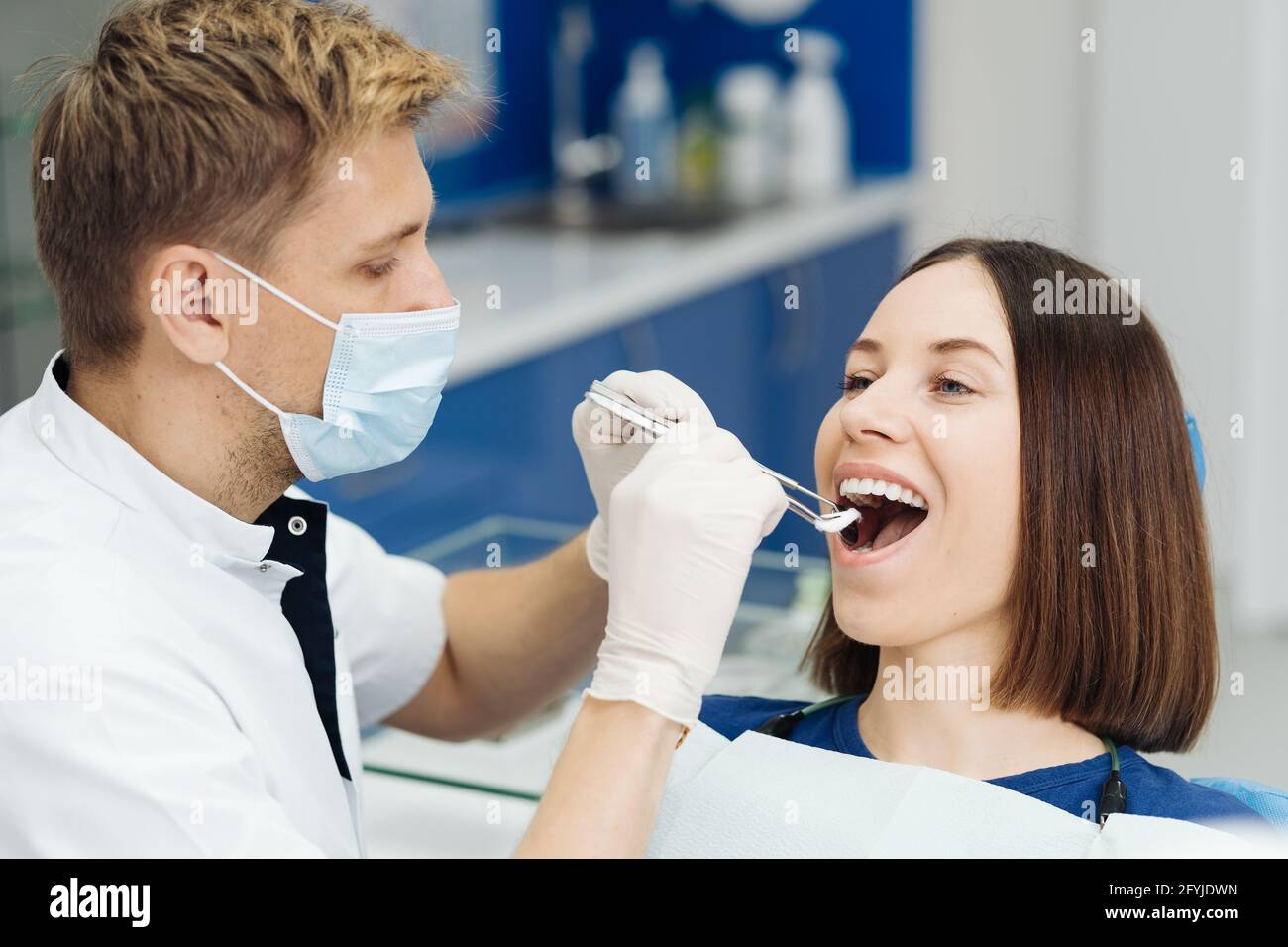 Caucasian male dentist examining young woman patient's teeth at dental ...