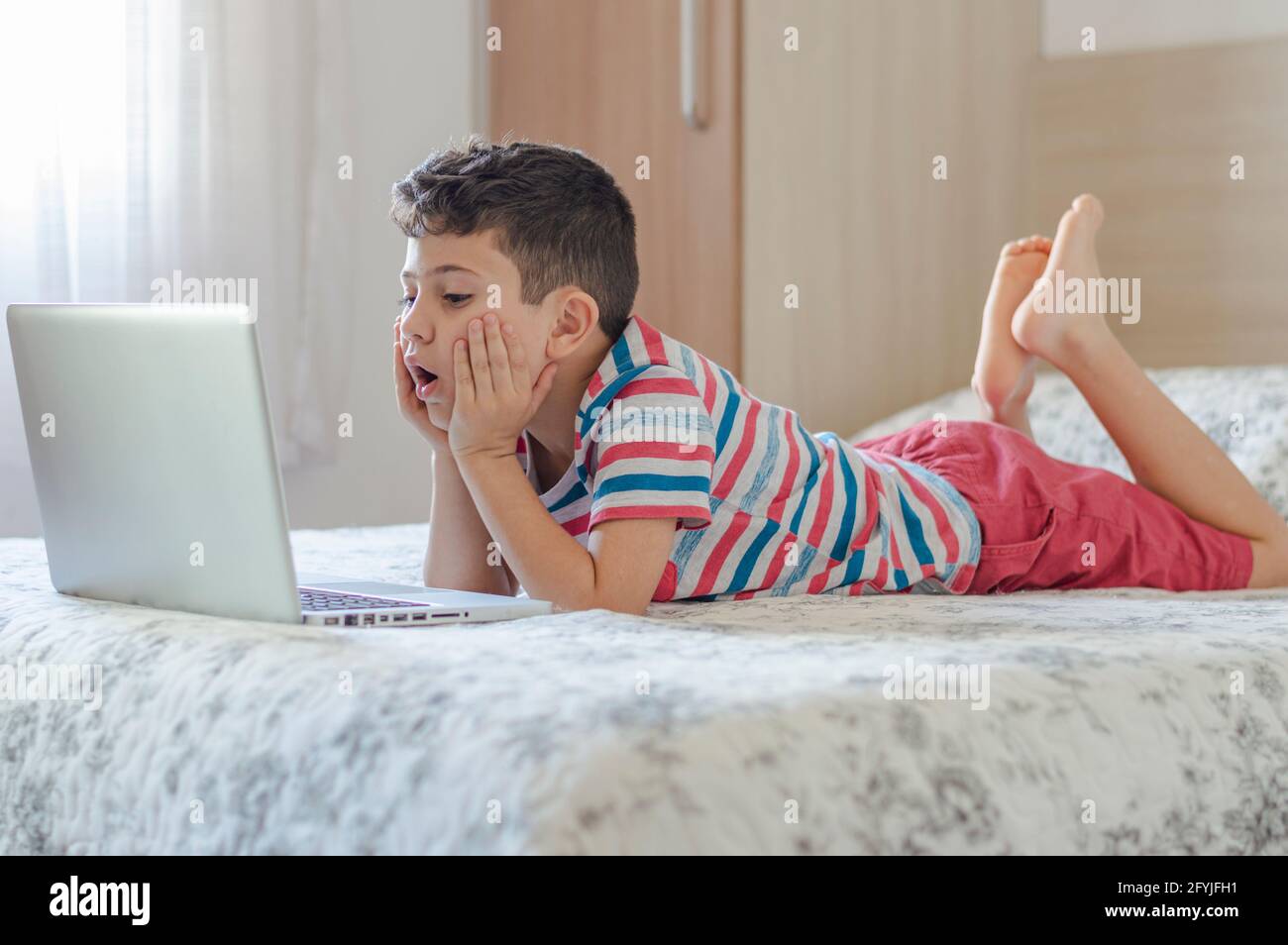 Young boy child lying on bed using a laptop. Online class lesson on ...
