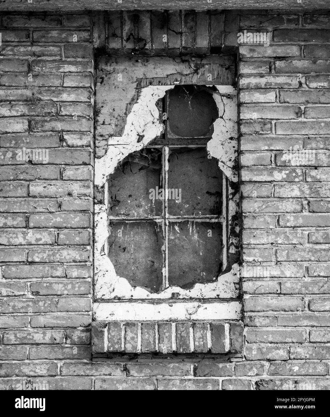 A monochrome image of a derelict window, boarded up, in a brick wall ...