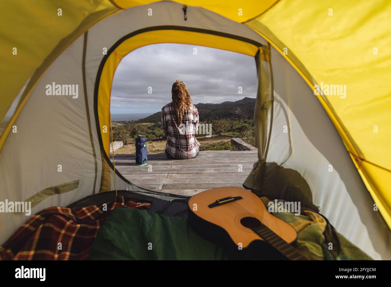 Rear view of caucasian woman camping, sitting outside tent on ...
