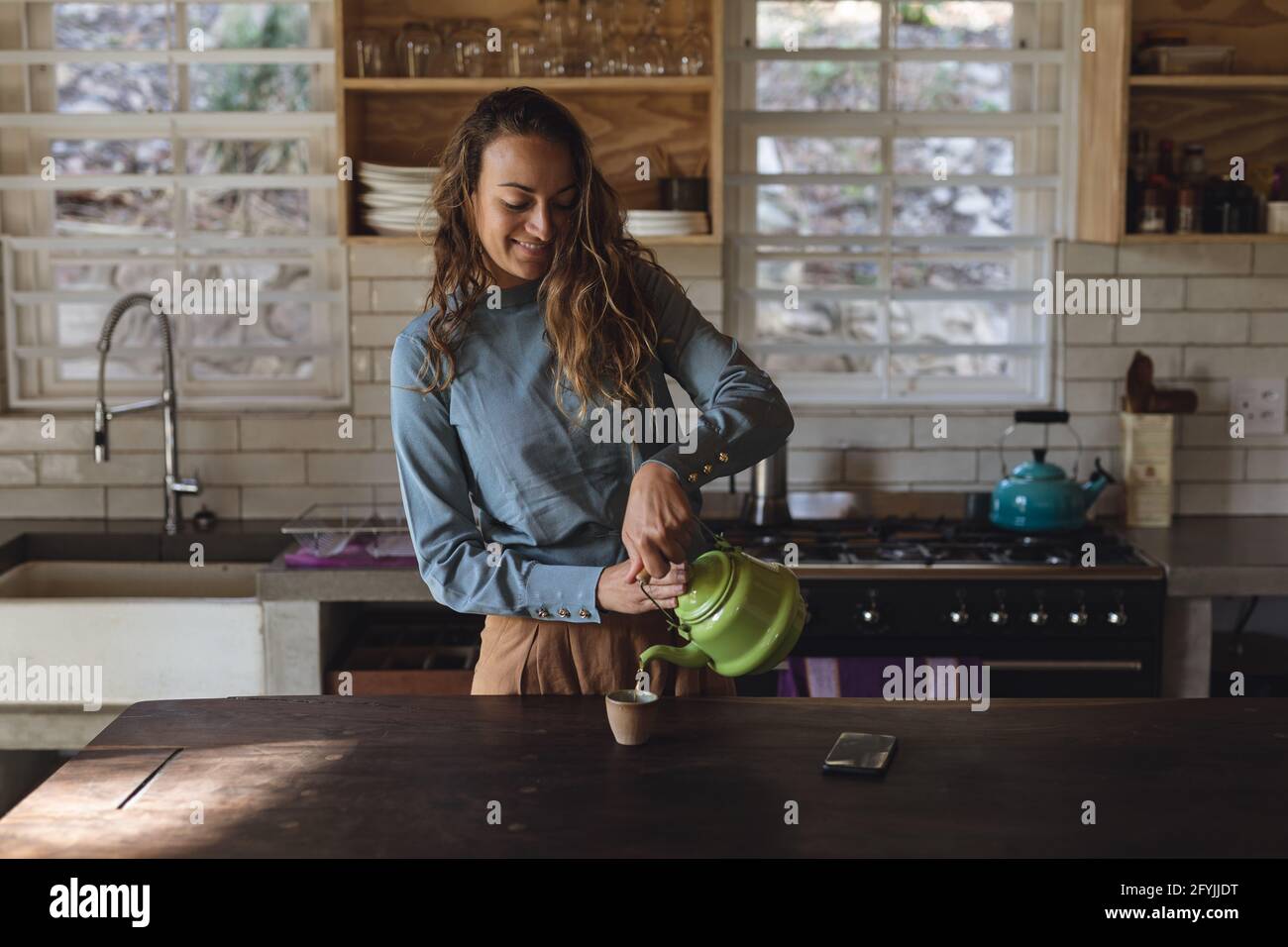 Happy caucasian woman standing in cottage kitchen pouring tea from ...