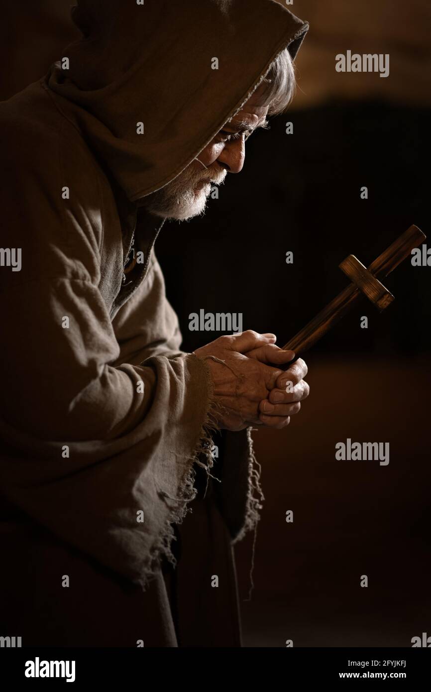 Old poor monk looks at the cross and doubts Stock Photo - Alamy
