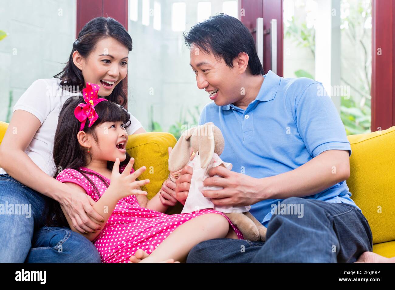 Chinese Family playing with daughter on sofa holding stuffed animal ...
