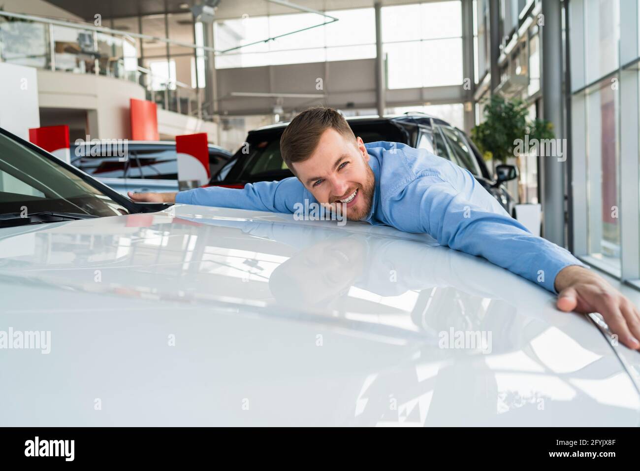 Handsome man hugging new car in dealership Stock Photo - Alamy