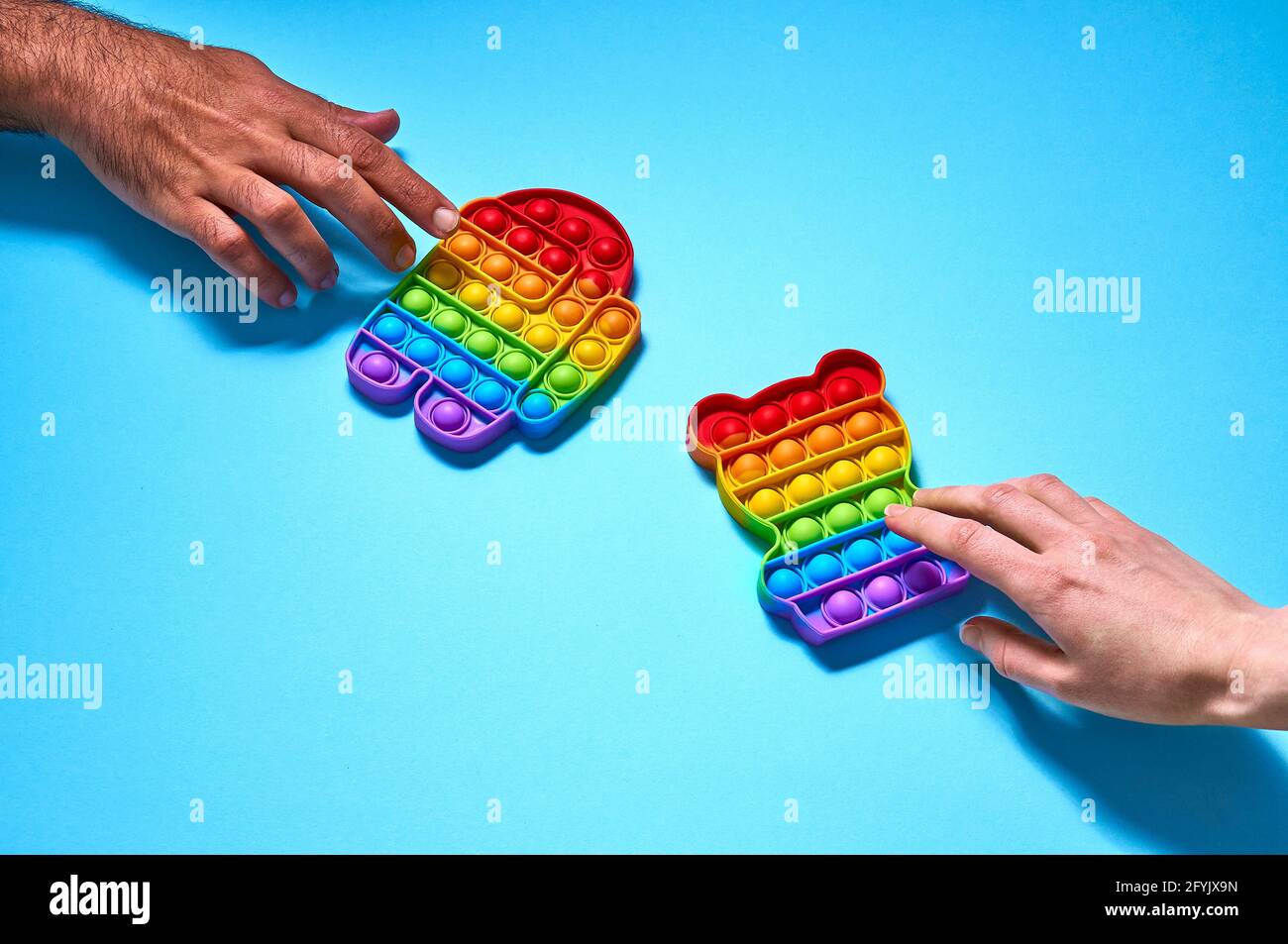 Woman and man hands reaches out to colorful trendy pop it toys on blue ...