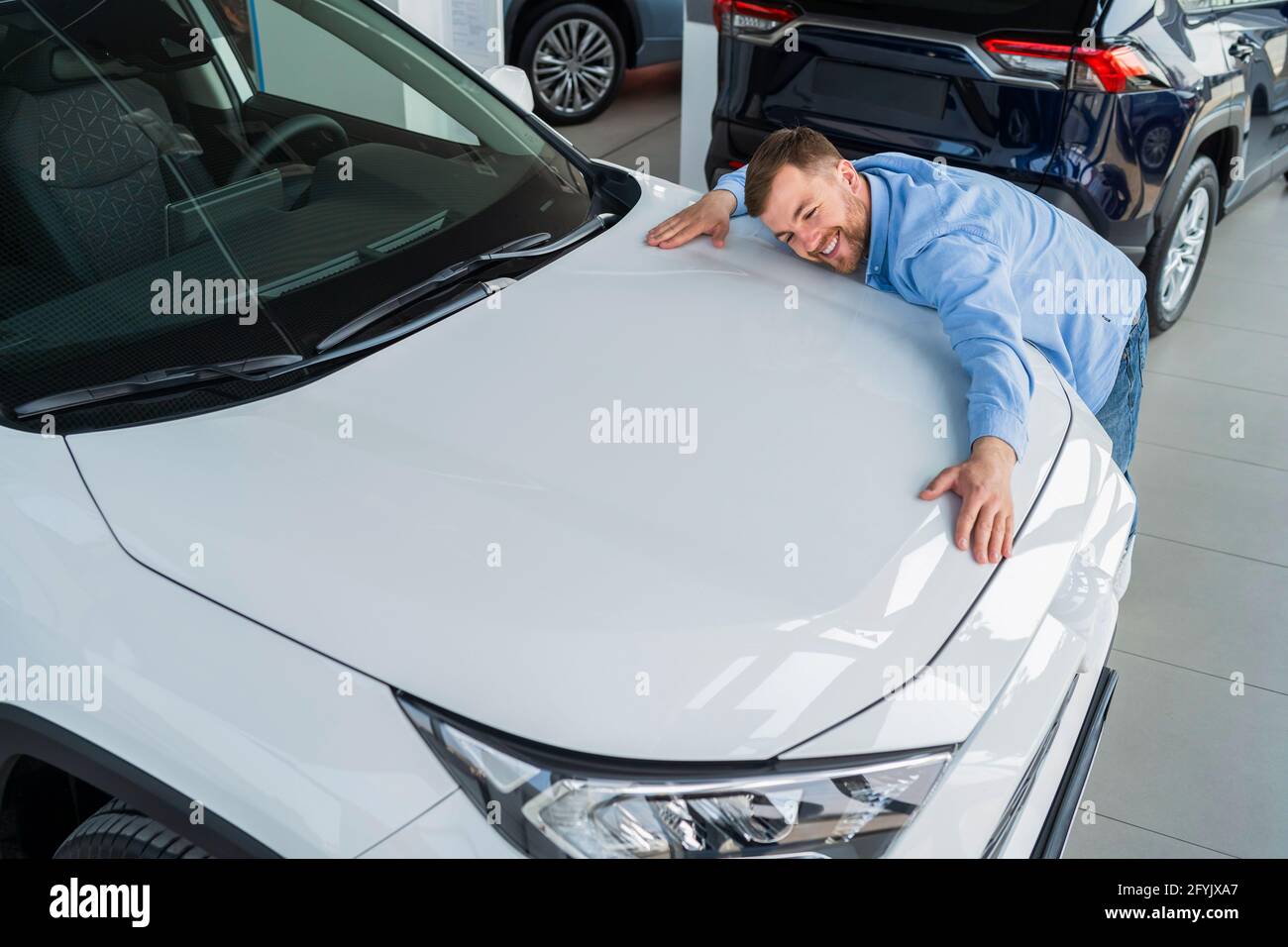 Handsome man hugging new car in dealership Stock Photo - Alamy