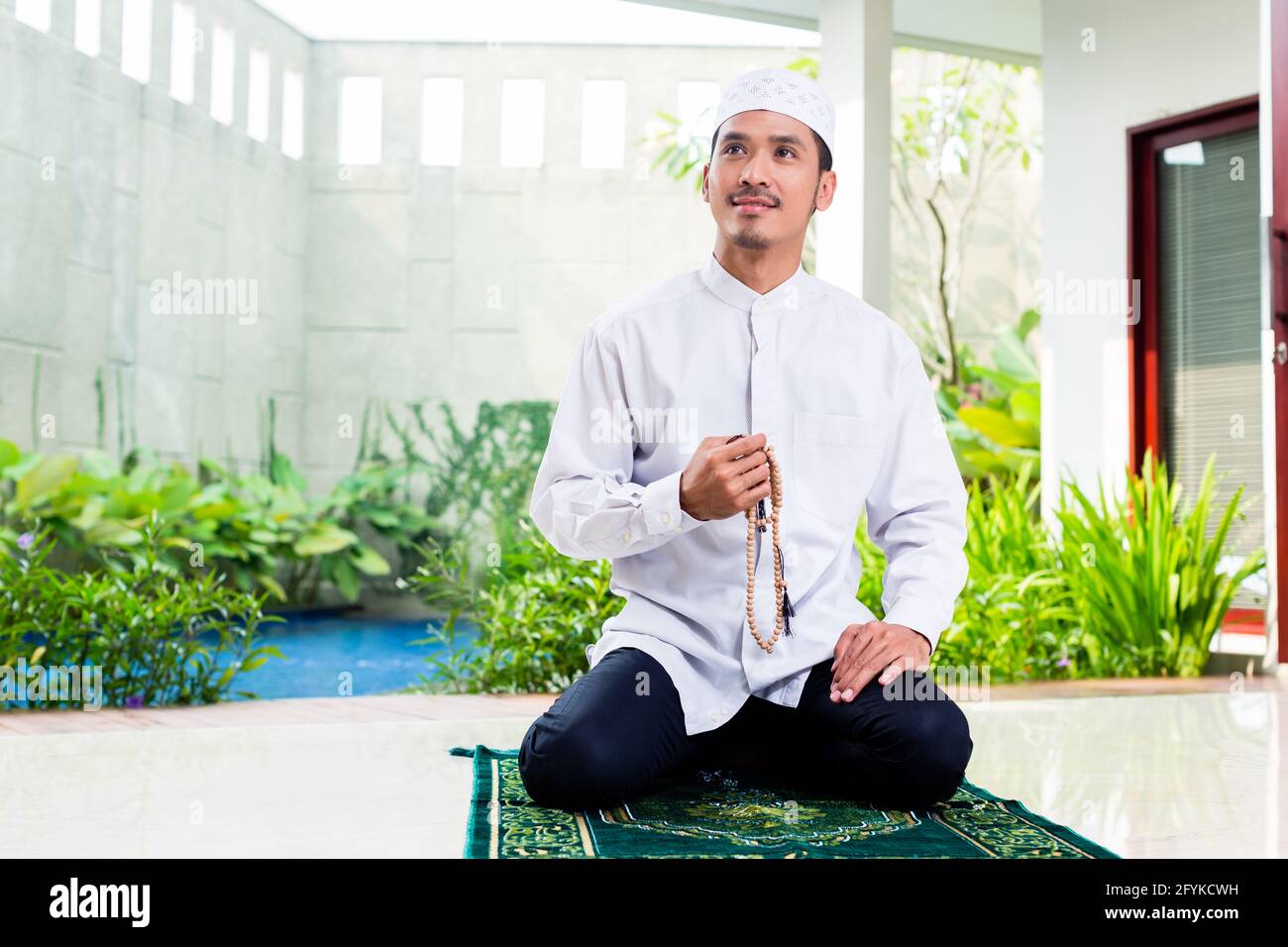 Asian Muslim man praying at home sitting on prayer carpet in his house ...
