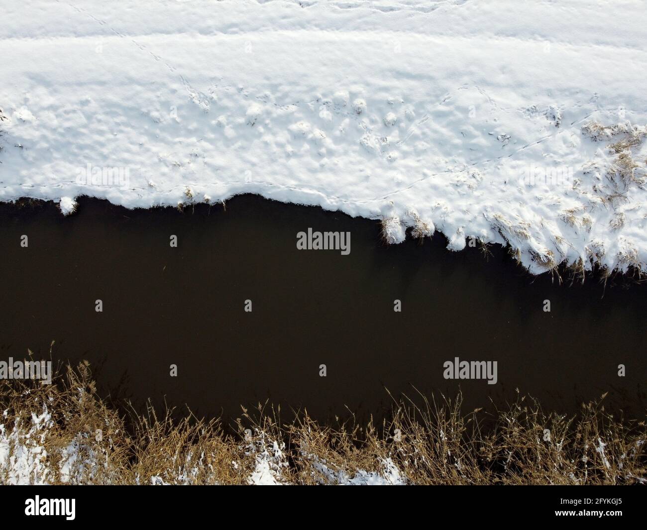 Top view of snow layer and dry grass on both sides of a winter river ...