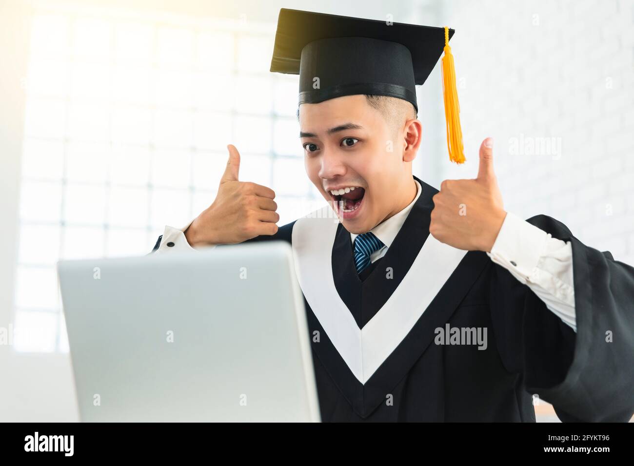 Happy male graduation watching the laptop and showing thumbs up Stock ...