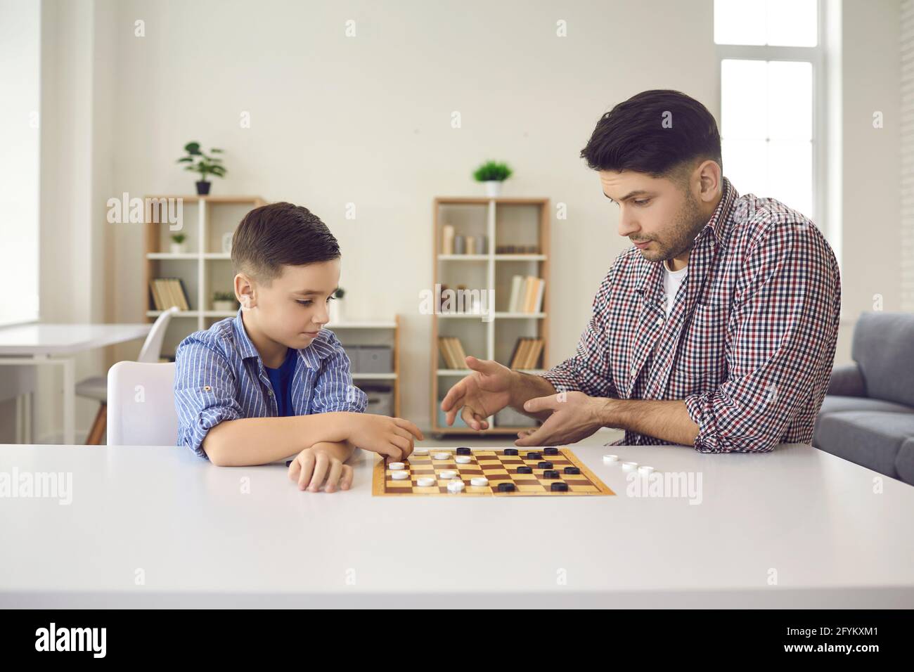 Portrait of concentrated father and son playing checkers sitting at ...