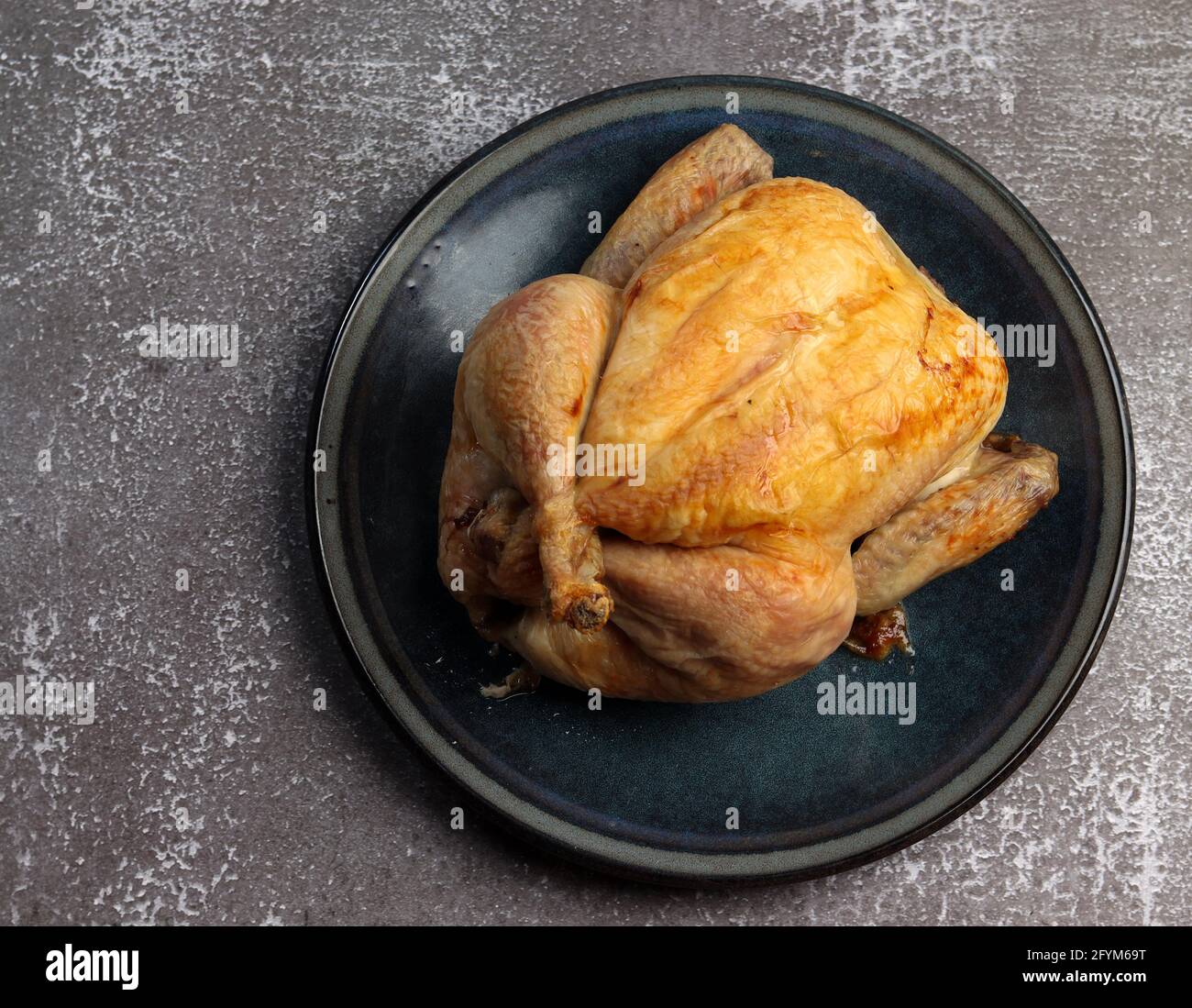 Baked whole chicken on a round plate on a dark background. Top view ...
