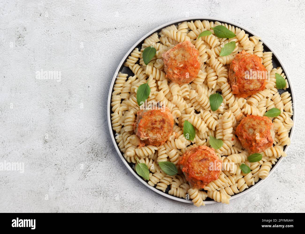 Pasta with meatballs in tomato sauce on a round plate on a light gray ...