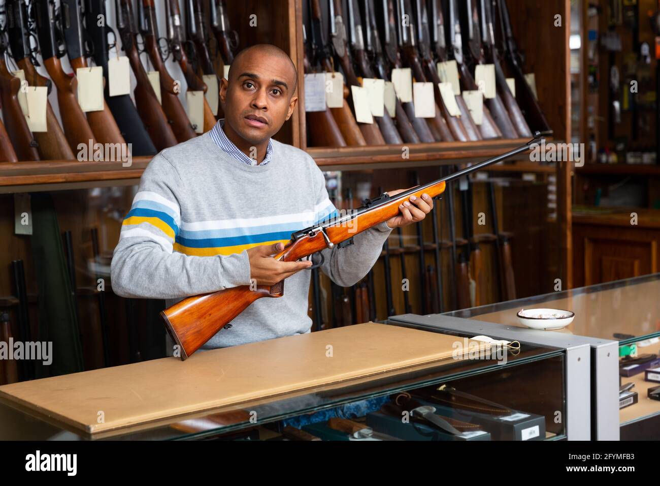 Hispanic salesman working behind counter of gun shop, showing hunting ...