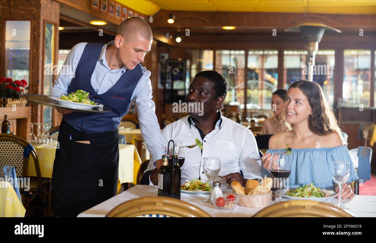 Elegant waiter serving company at restaurant, bringing food for man and ...