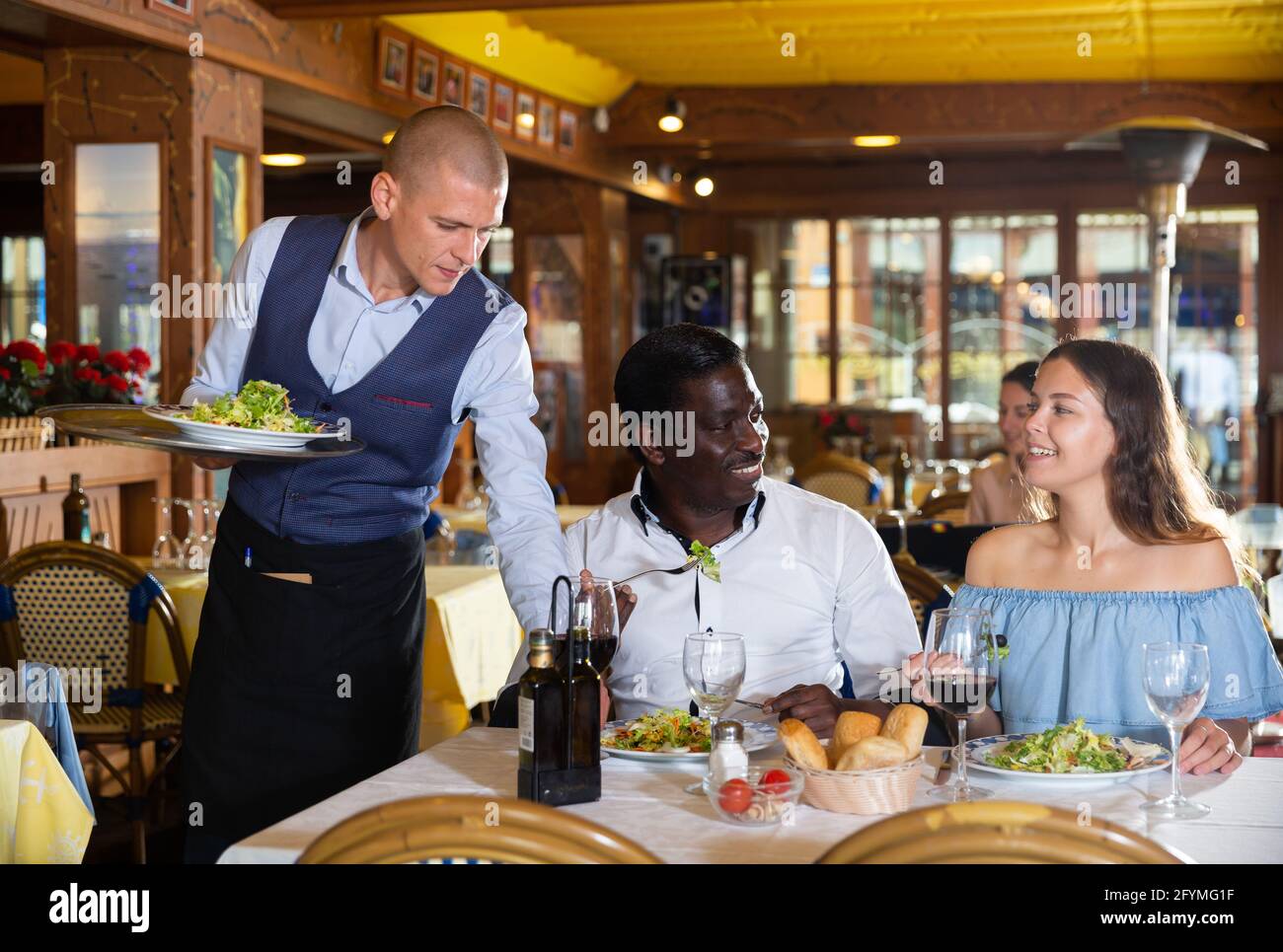 Positive male waiter writing down order from visitors in restaurant ...