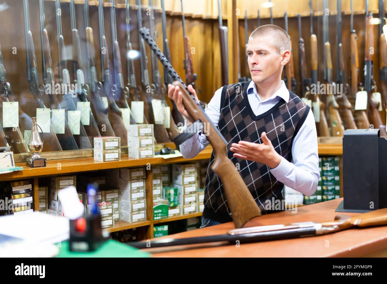 Confident seller of armory shop offering collection submachine gun with ...