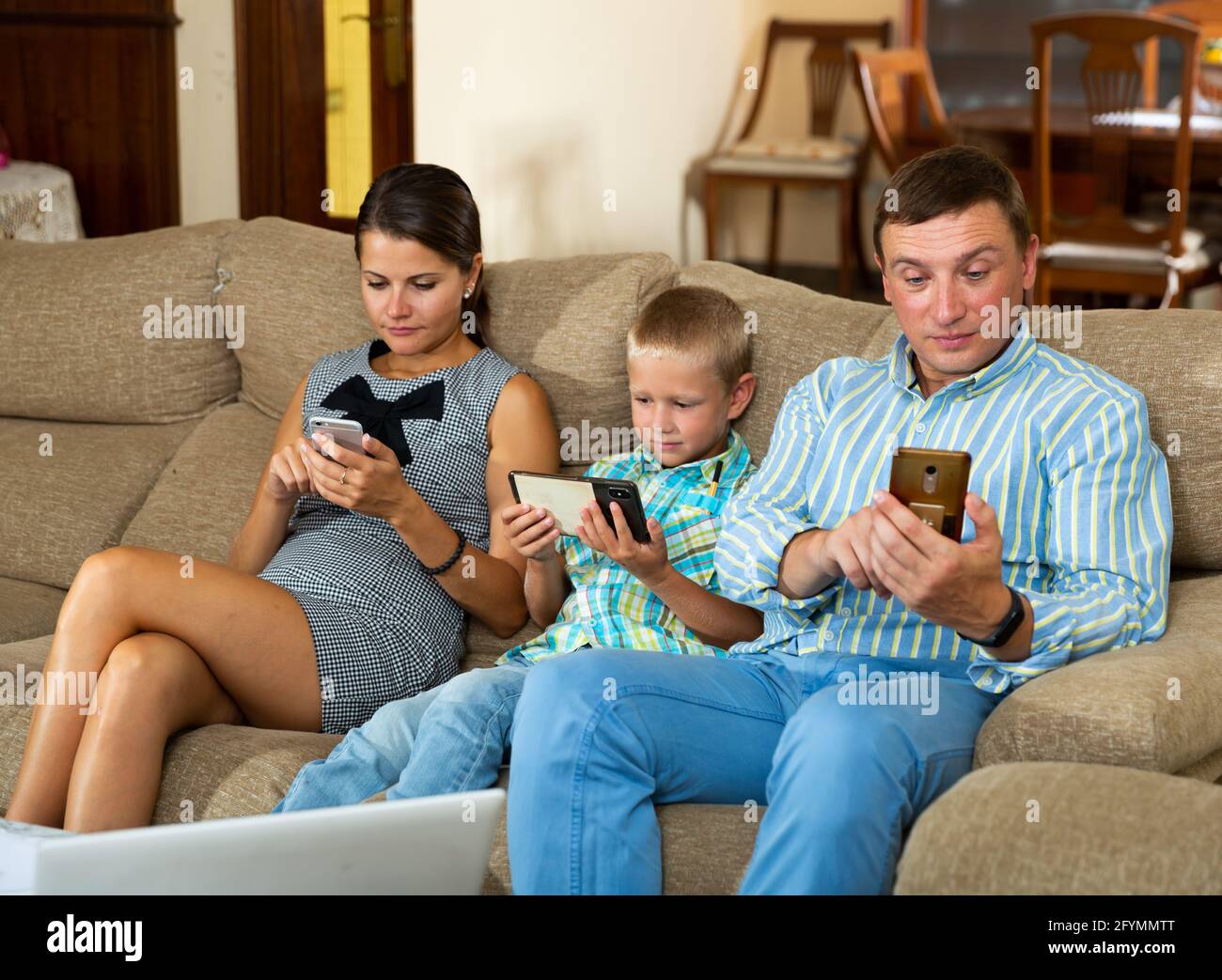 Portrait of young family and his son using phones at home interior ...