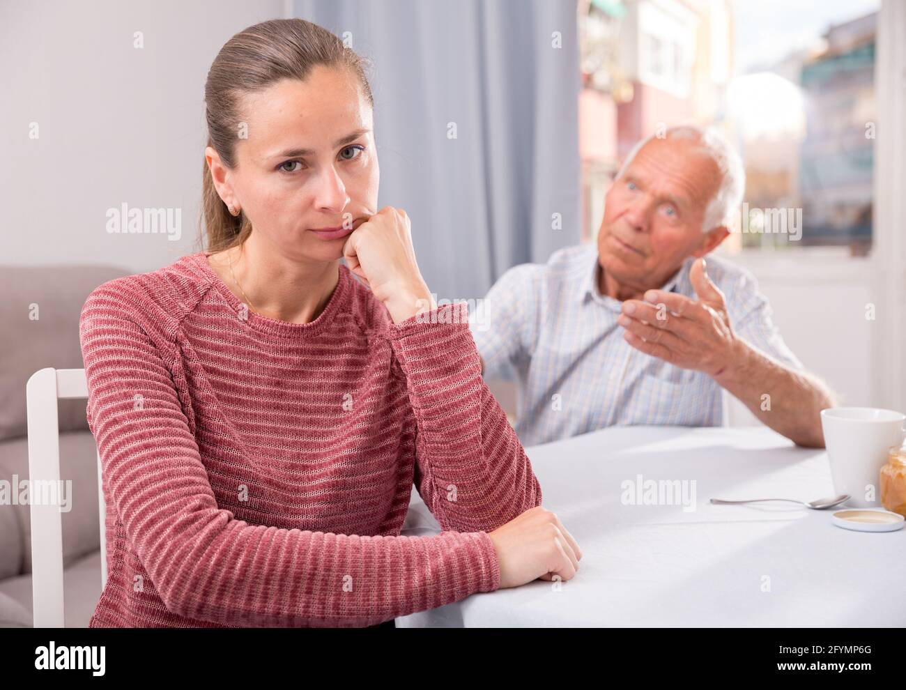 Portrait of upset young woman sitting after quarrel with father at home ...