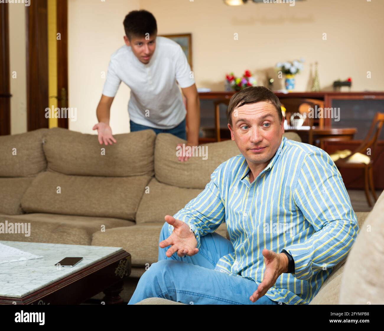 Upset father sitting while quarreling with his teenage son in domestic ...
