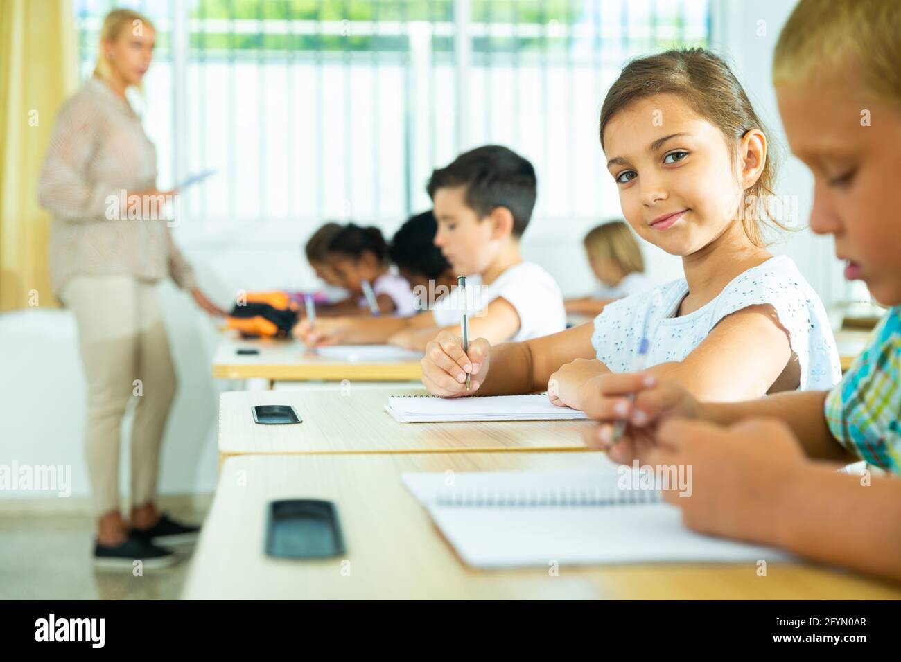 Portrait of positive tween schoolgirl sitting on lesson in classroom ...