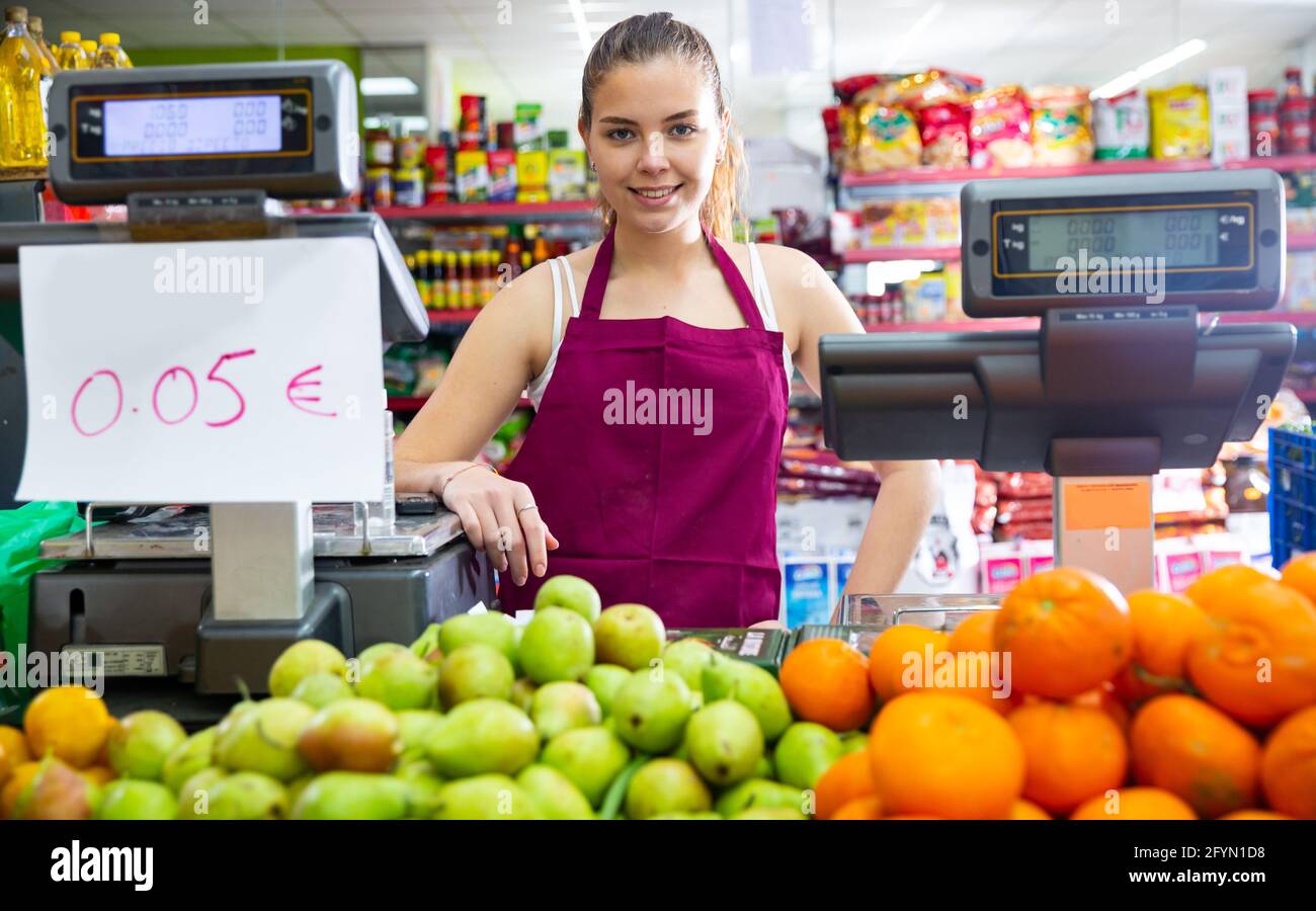 Portrait of young female shop assistants laying out and weighing fruit ...