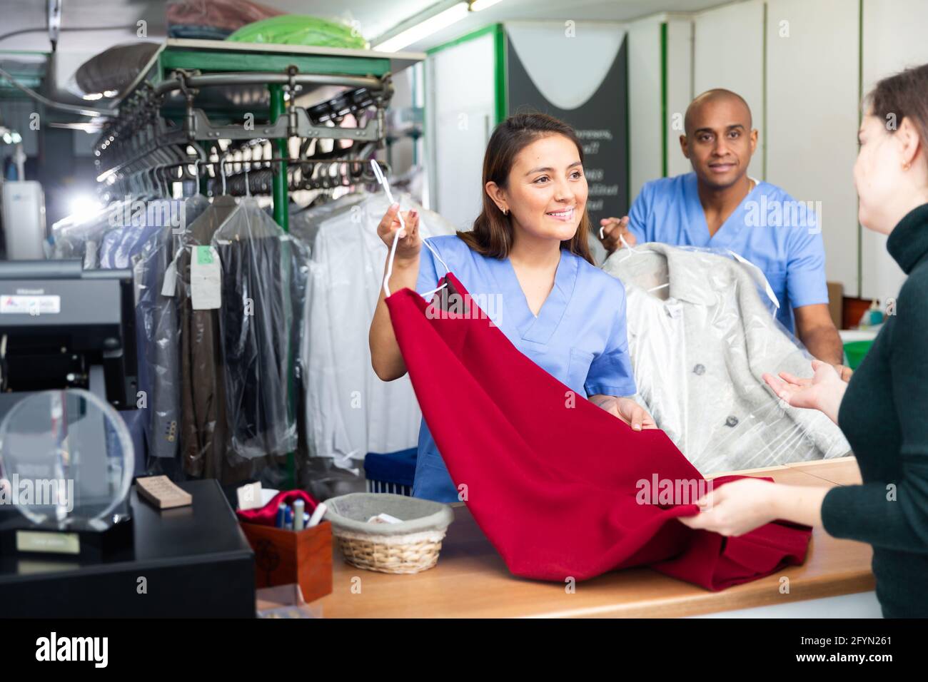 Cheerful woman laundry worker returning clean clothes to customer at ...