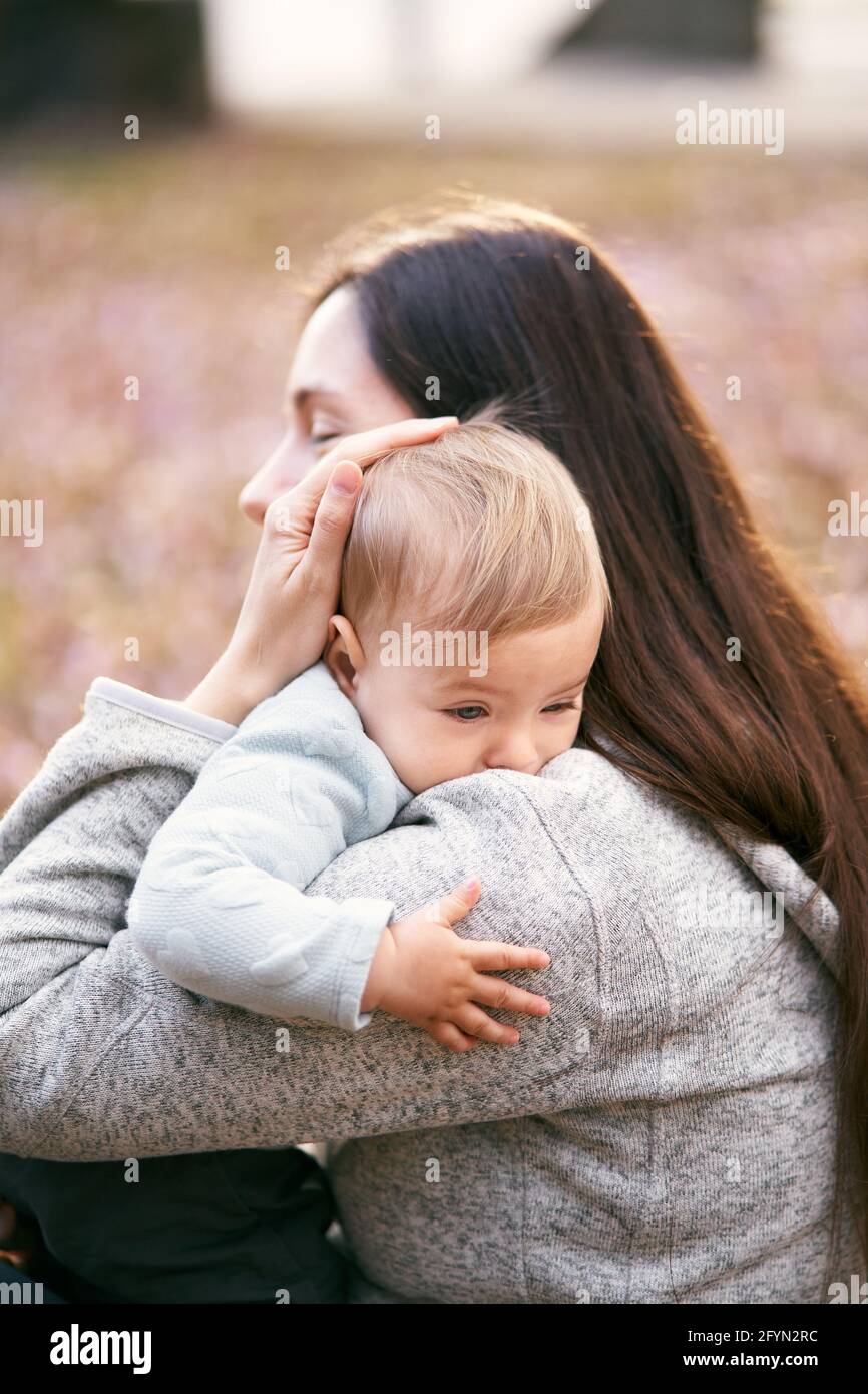 Mom hugs the baby to her chest, sitting on the foliage in the park ...