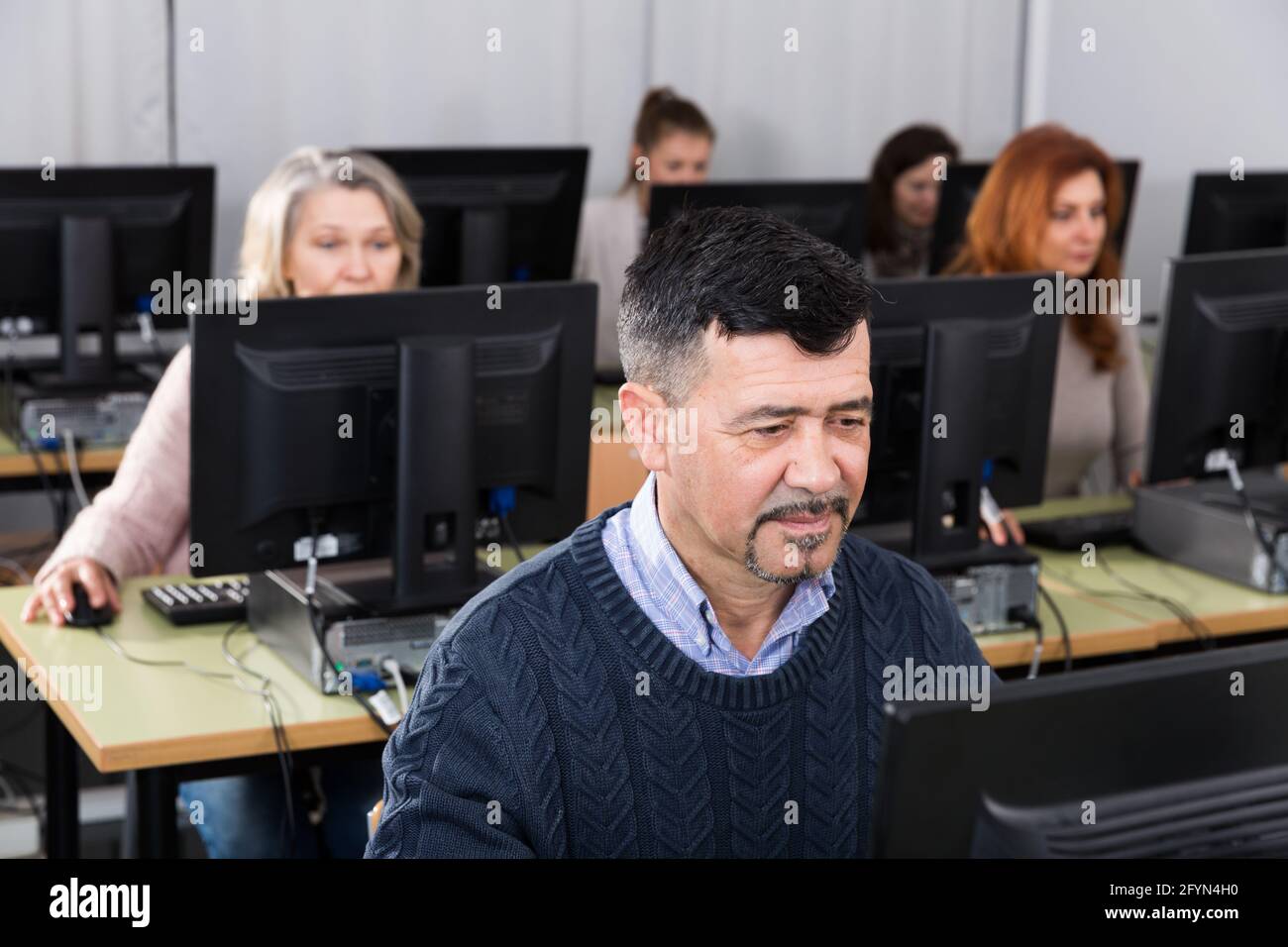 Positive middle aged man taking computer lessons with group of elderly ...