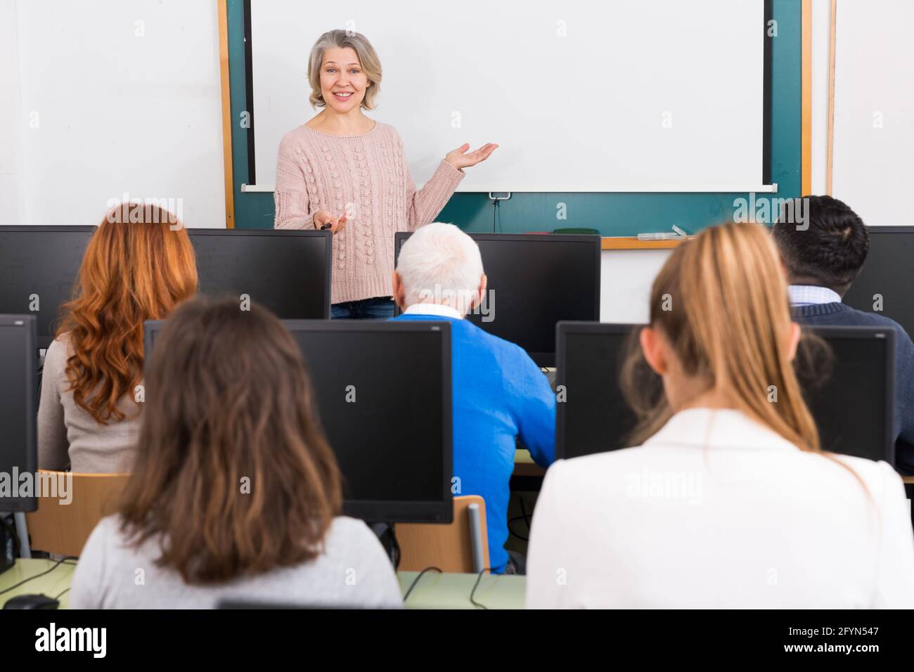 Smiling mature female coach lecturing adult students of different age ...