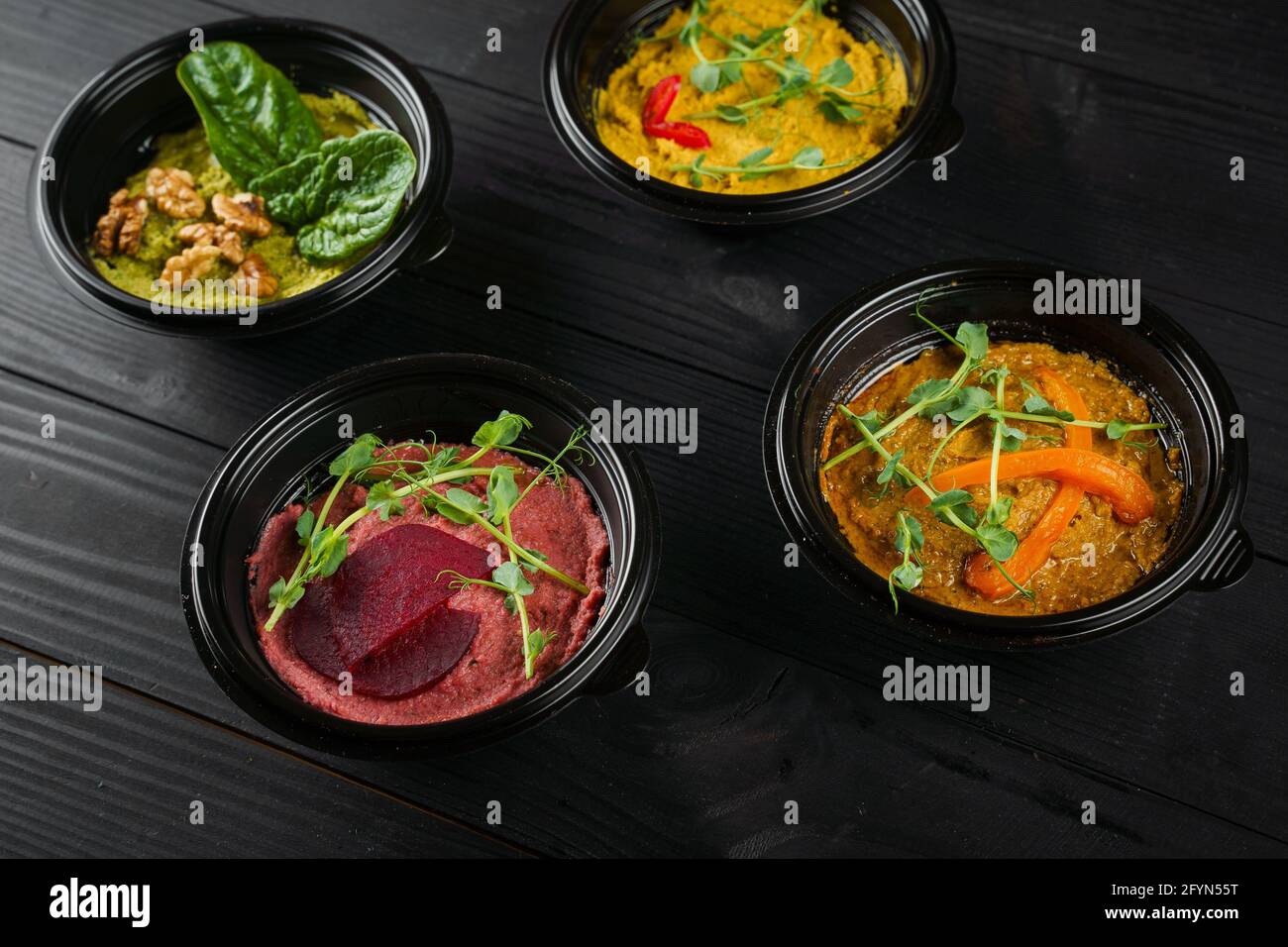 Hummus garnished peppers, chili, beet and herbs in black bowl on dark ...
