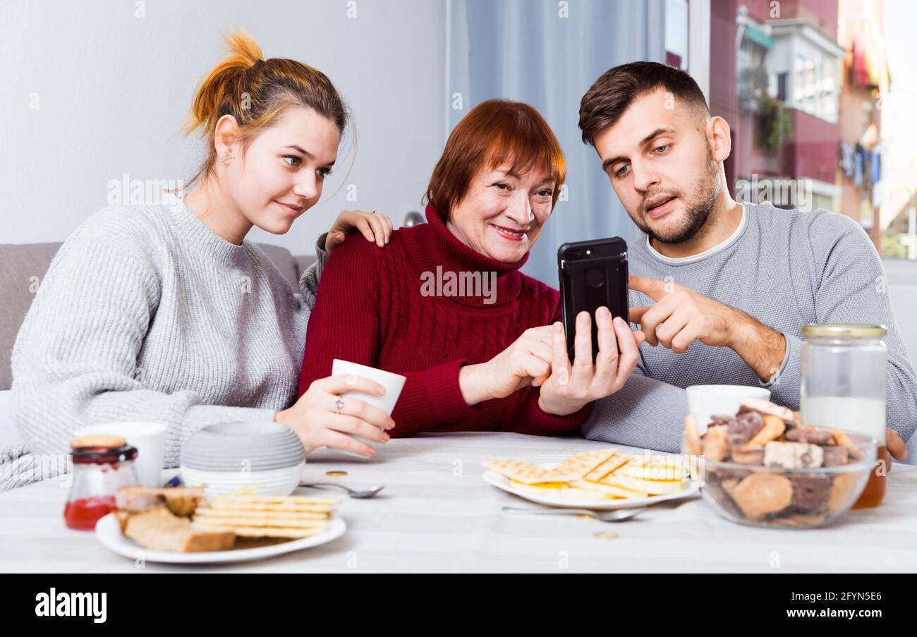 Happy senior woman with young couple absorbedly looking at phone at ...