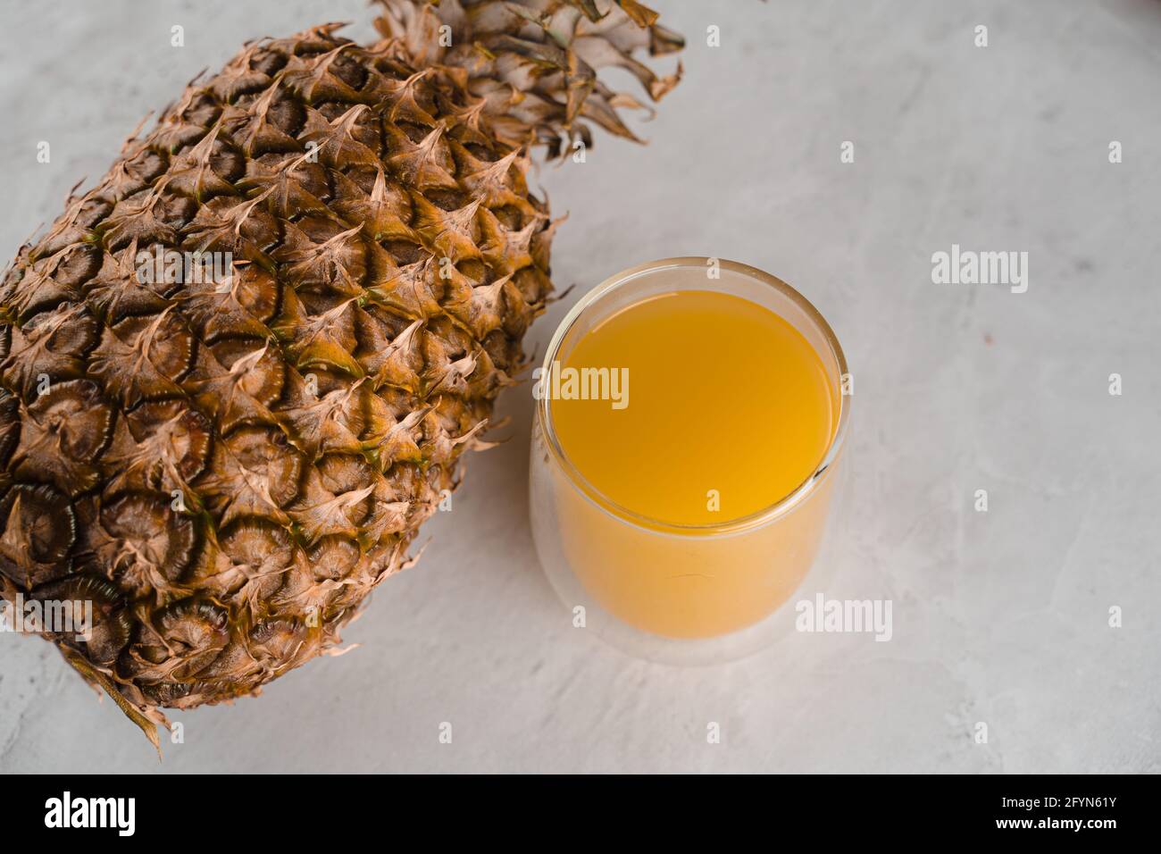Pineapple fruit and juice in double glass cup on white stone background ...